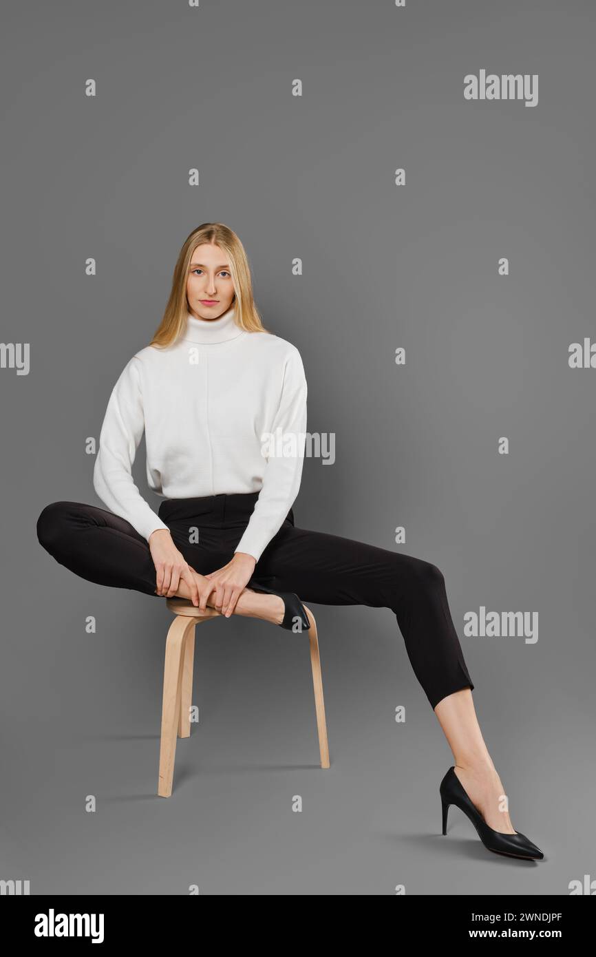 Long-legged blonde woman woman in tight trousers and sweater sitting on ...