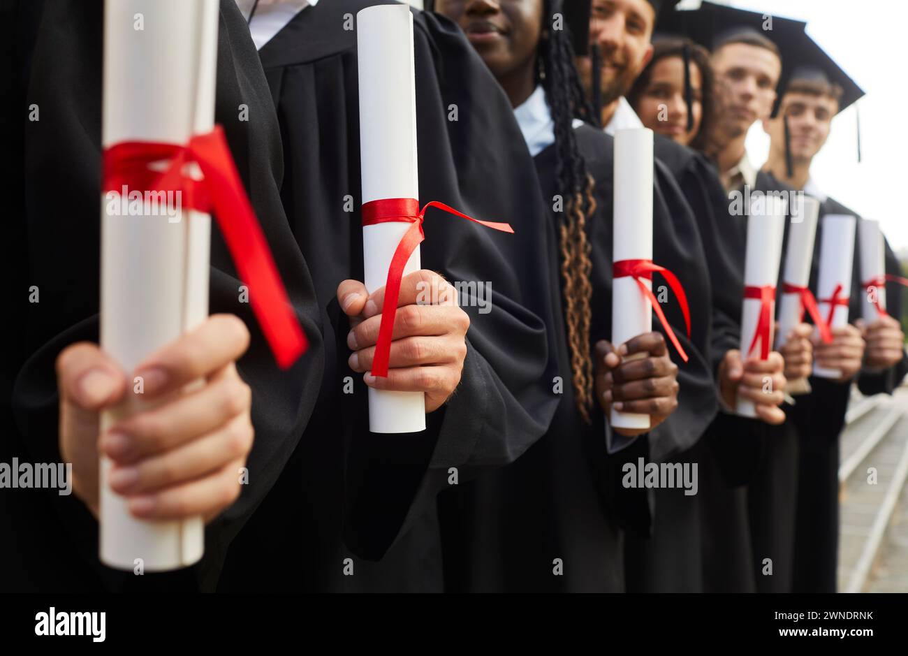 Graduate students standing in a row in black robes with diplomas in ...