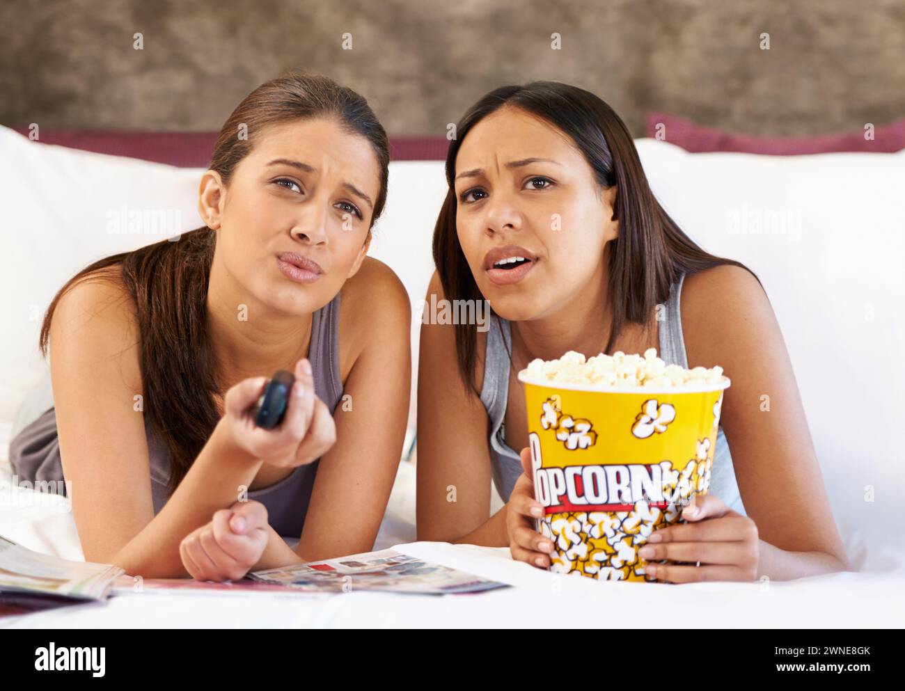 Television, remote control and confused women on a bed with popcorn ...