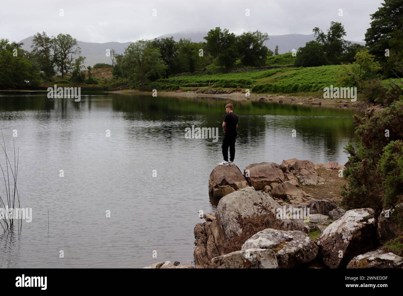 Fisherman fishing on a secluded lake on a gloomy day Stock Photo - Alamy