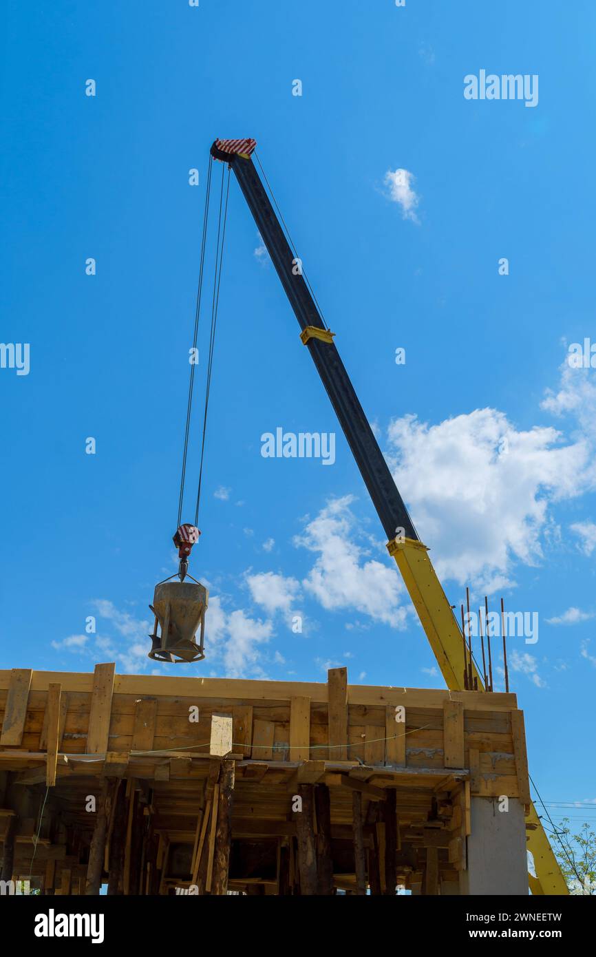 An aerial crane lifts concrete bucket for pouring concrete cement mix into formwork at ...