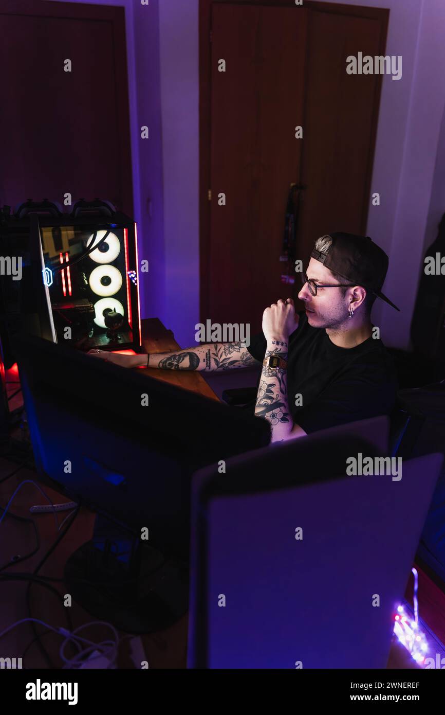 Side view of a concentrated young gamer wearing glasses using computer ...