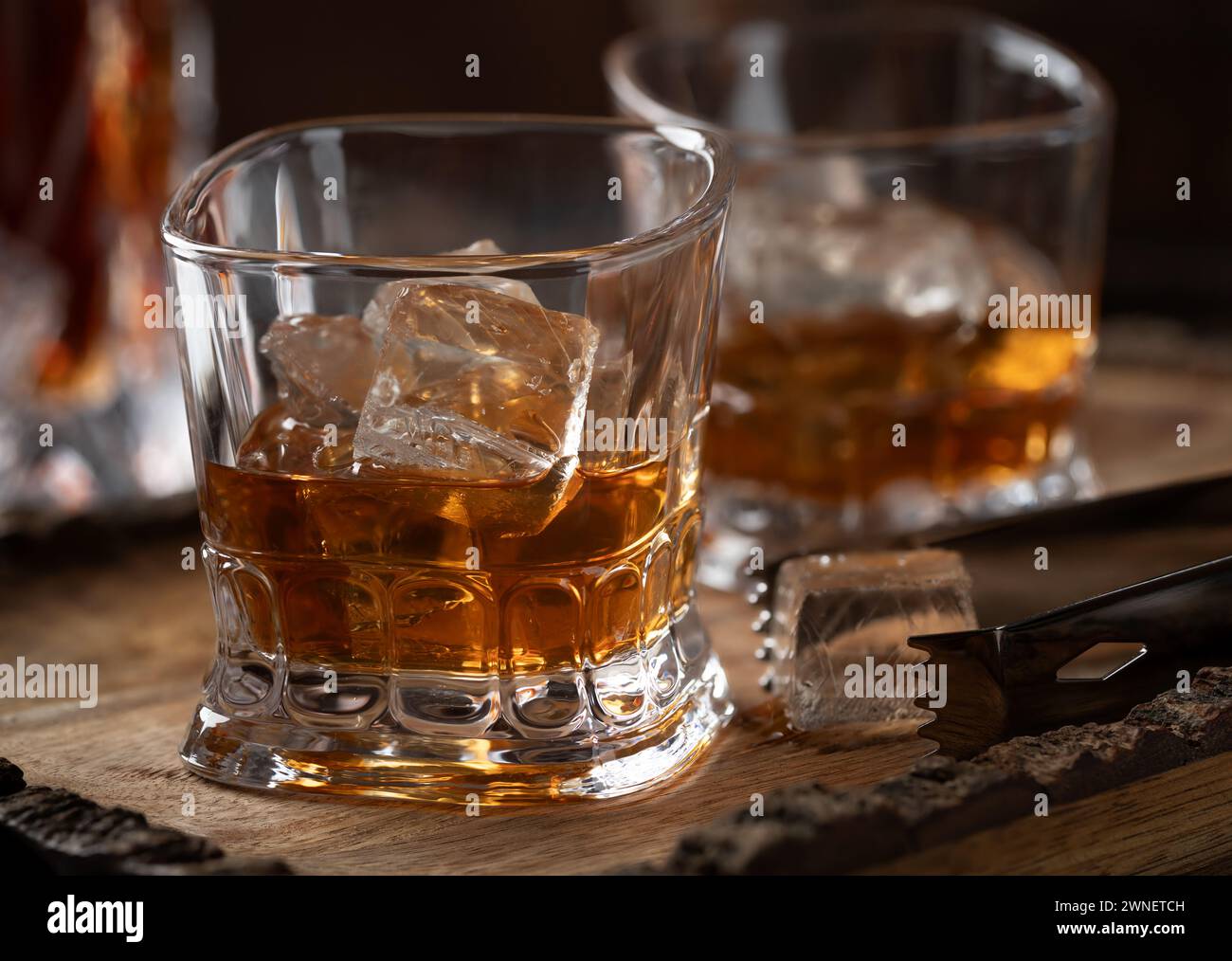 Two glasses of whiskey with ice on rustic wooden tray with decanter in ...