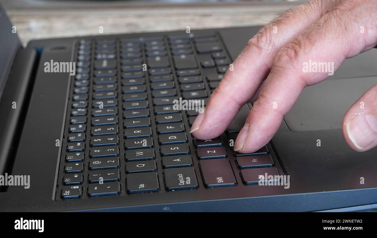 A close-up view of a senior mans hands as he types on a laptop located ...