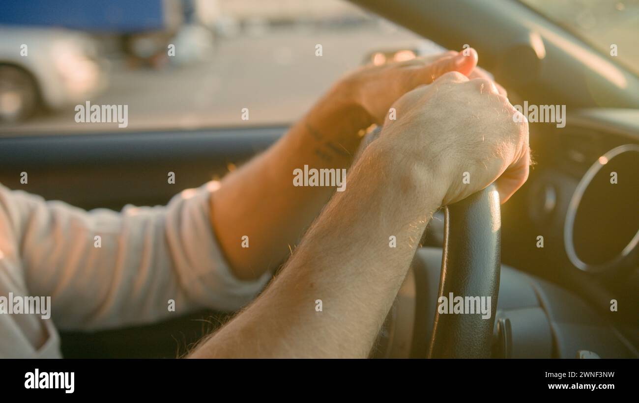 Close up male hands turning steering wheel driving vehicle in sunset ...
