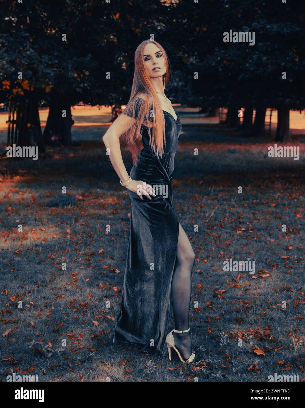 On fire, a model poses in a long dress with trees in the background ...