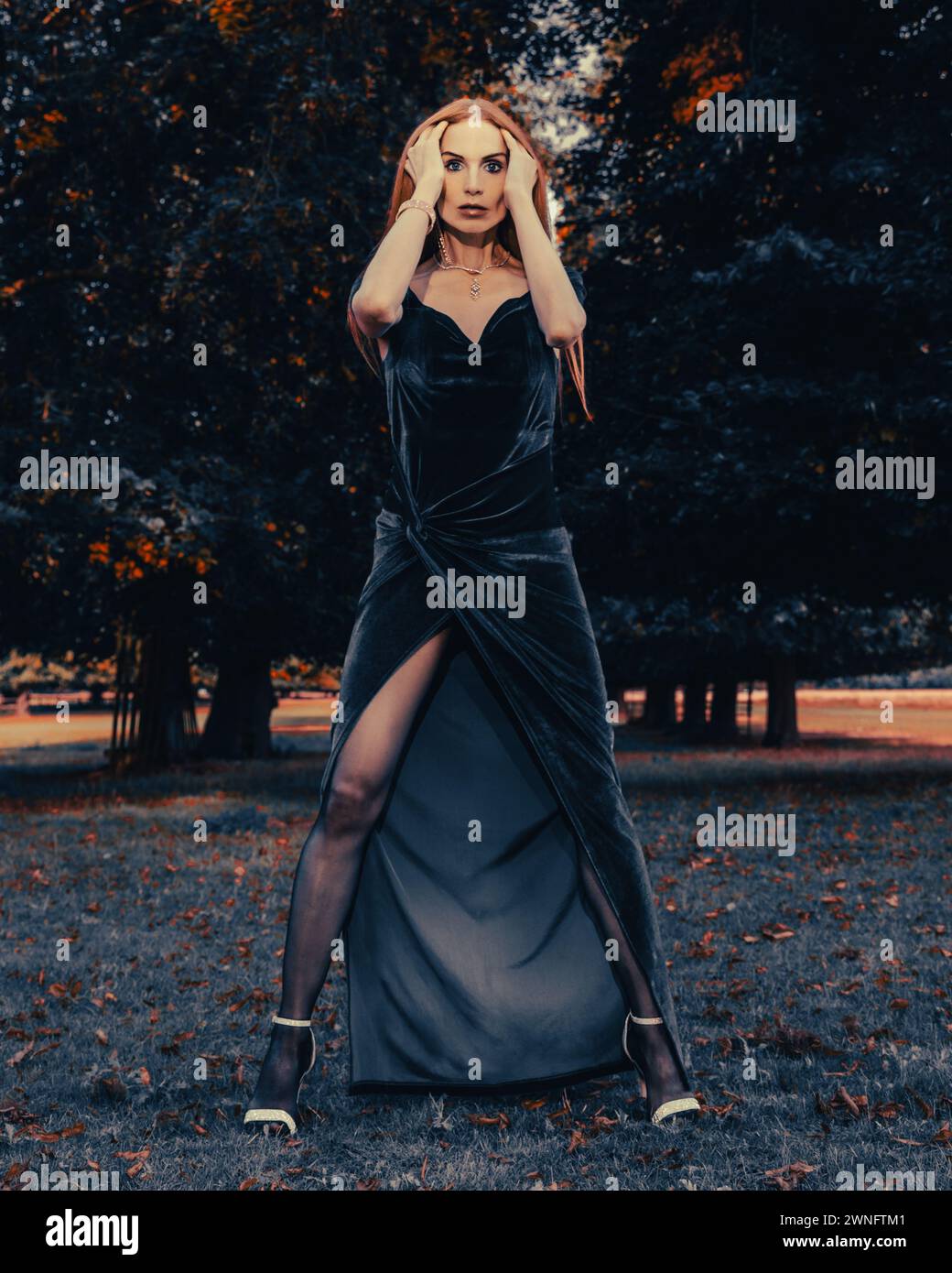 On fire, a model poses in a long dress with trees in the background ...