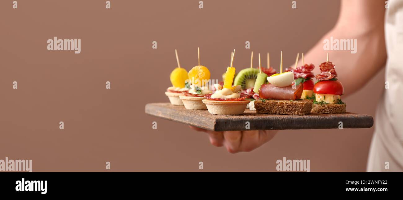 Waiter holding board with tasty canapes on brown background with space ...