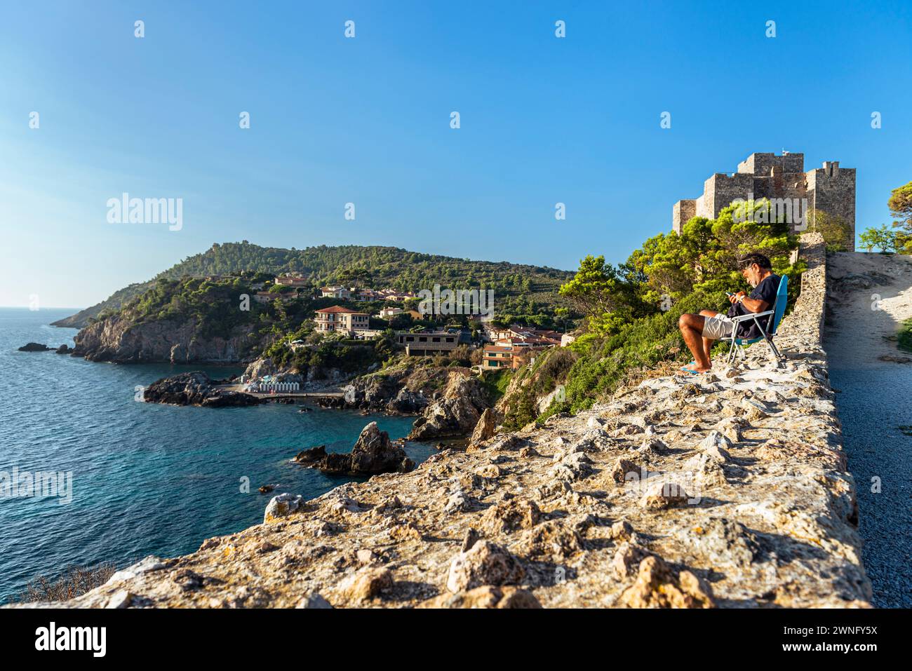 A man sitting on a chair on the wall of the Rocca Aldobrandesca castle ...