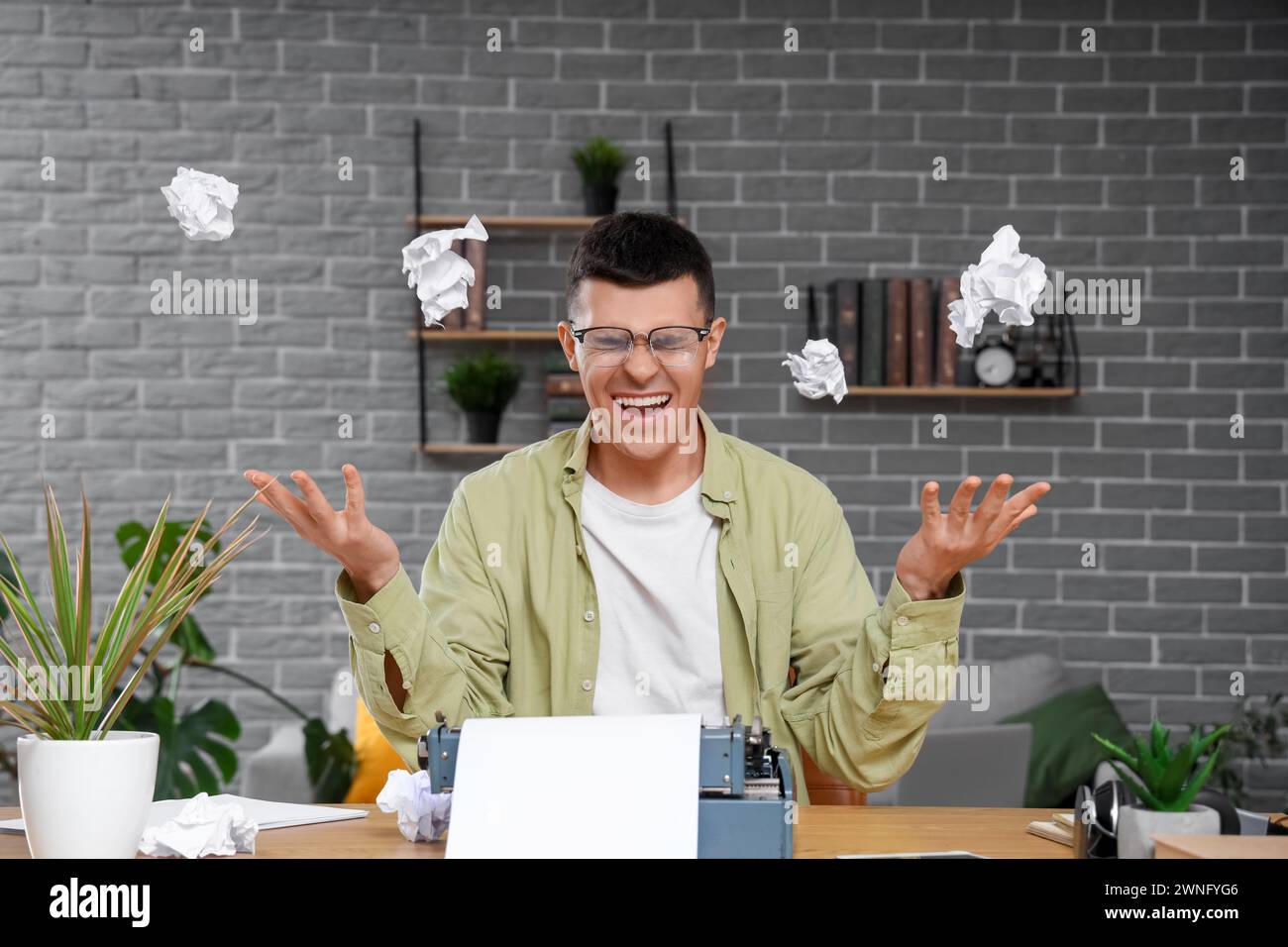 Angry young author with crumpled paper and vintage typewriter at table ...