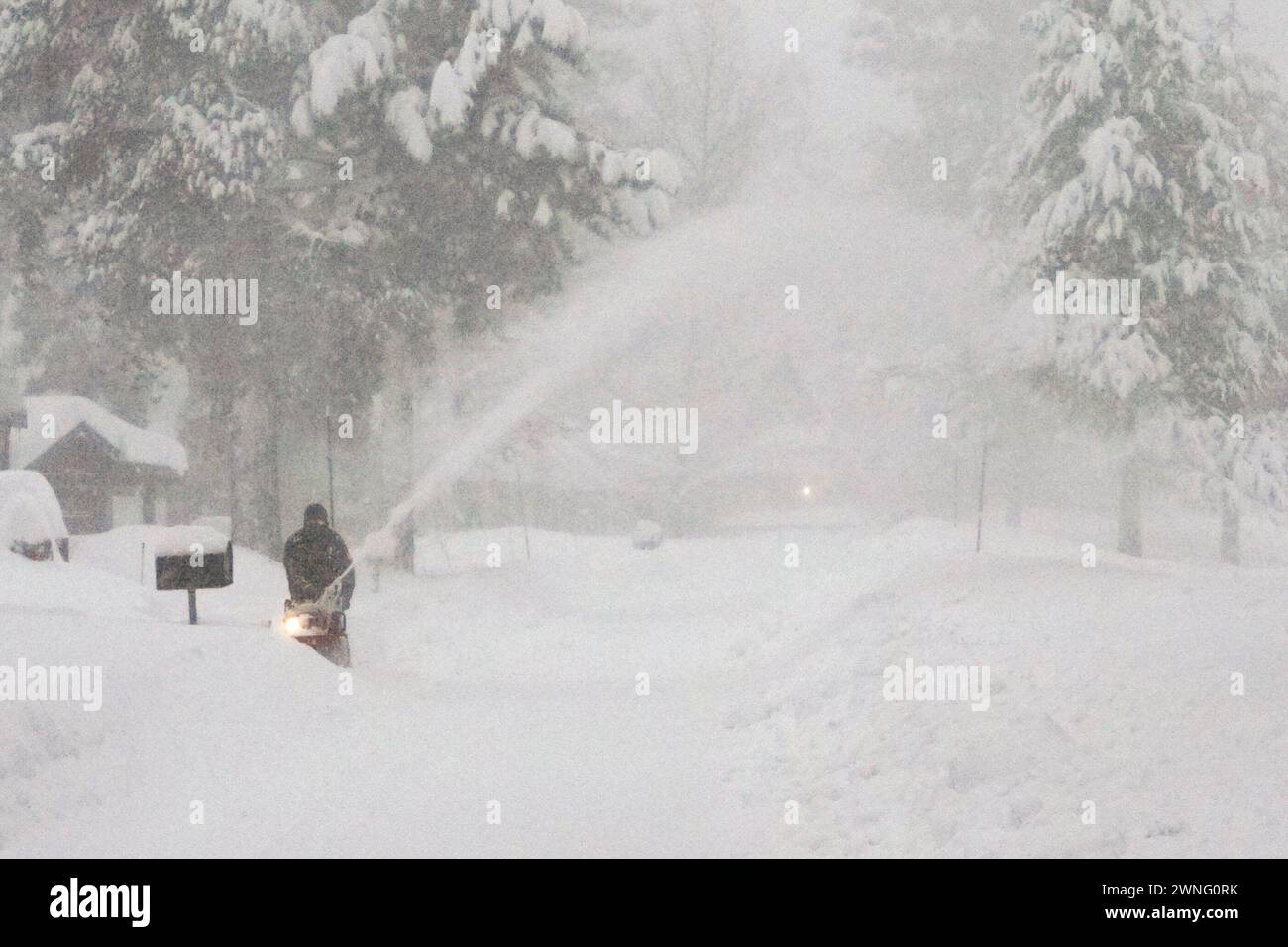 A person uses a snow blower to clear snow from a driveway during a ...