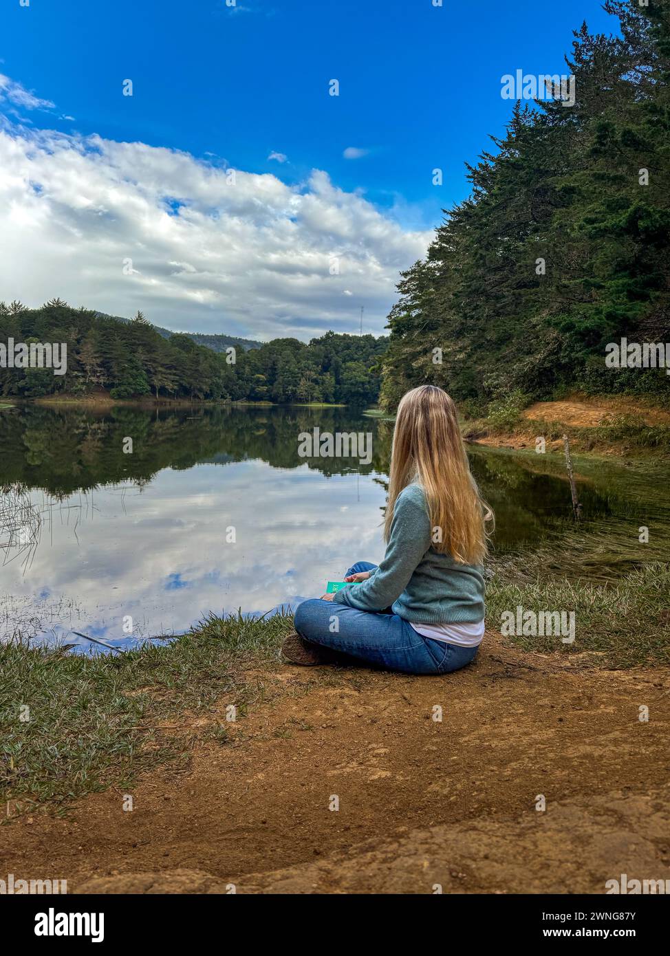 Beautiful blonde woman sitting next to a lake in the forest of Costa ...