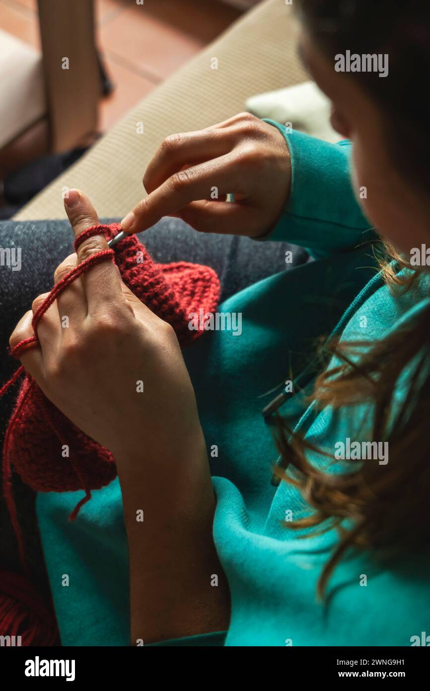 Young Caucasian woman knitting a scarf with red yarn. Sitting on the ...