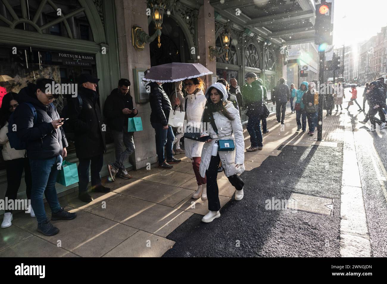 Pedestrians shelter under umbrellas whilst making their way along past Fortnum & Mason ...