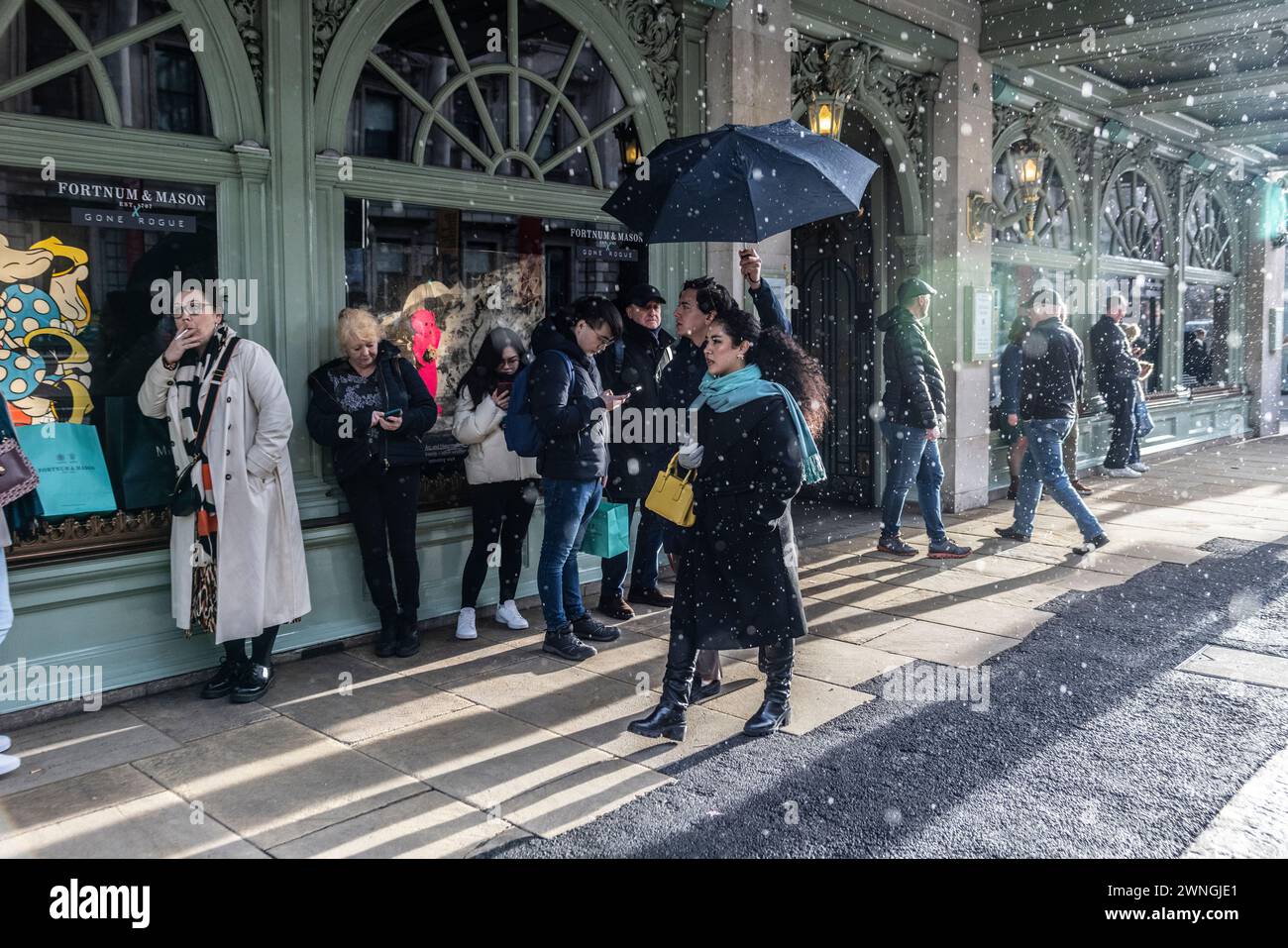 Pedestrians shelter under umbrellas whilst making their way along past Fortnum & Mason ...
