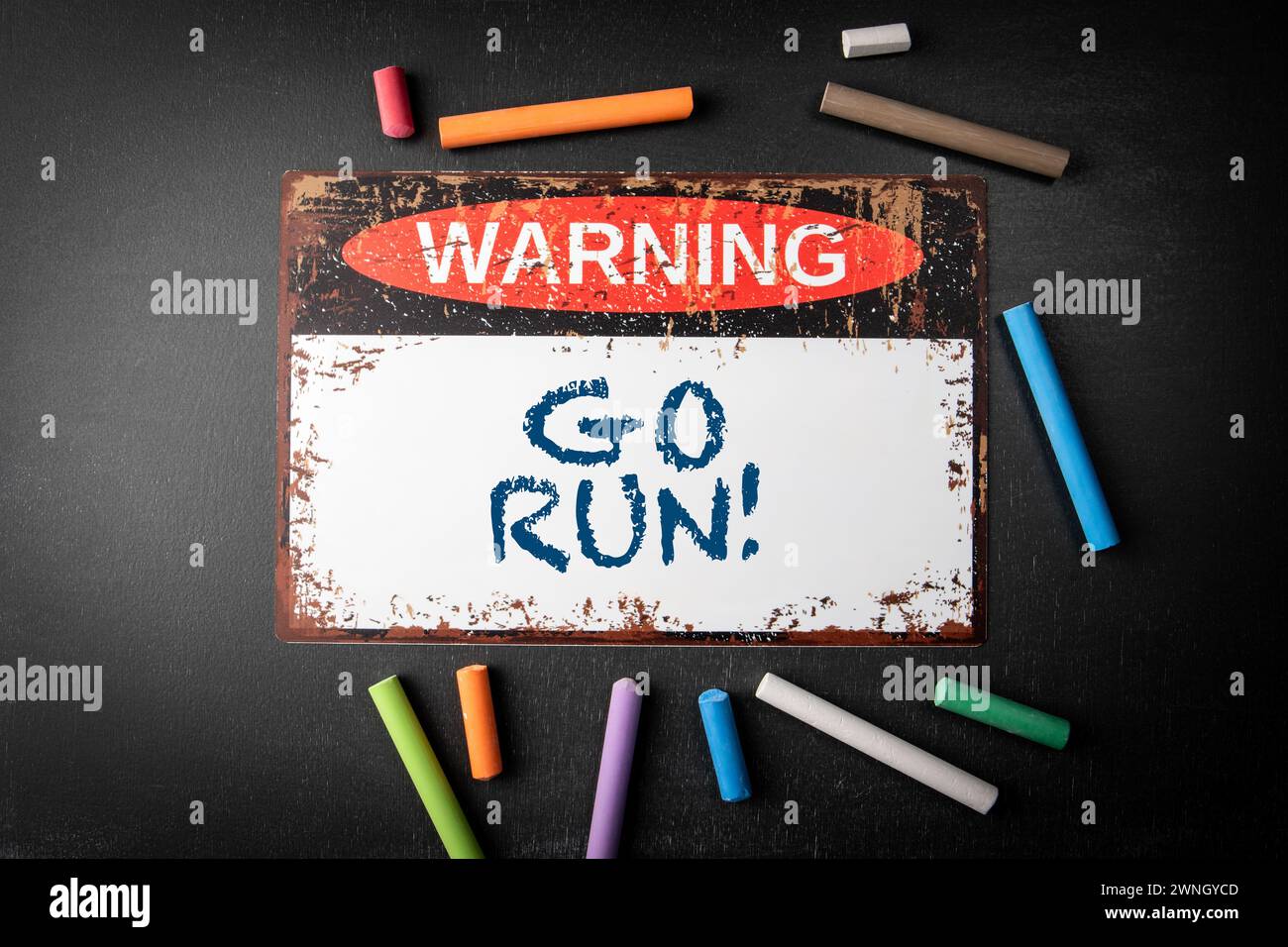 Go Run. Metal warning sign and colored pieces of chalk on a dark ...