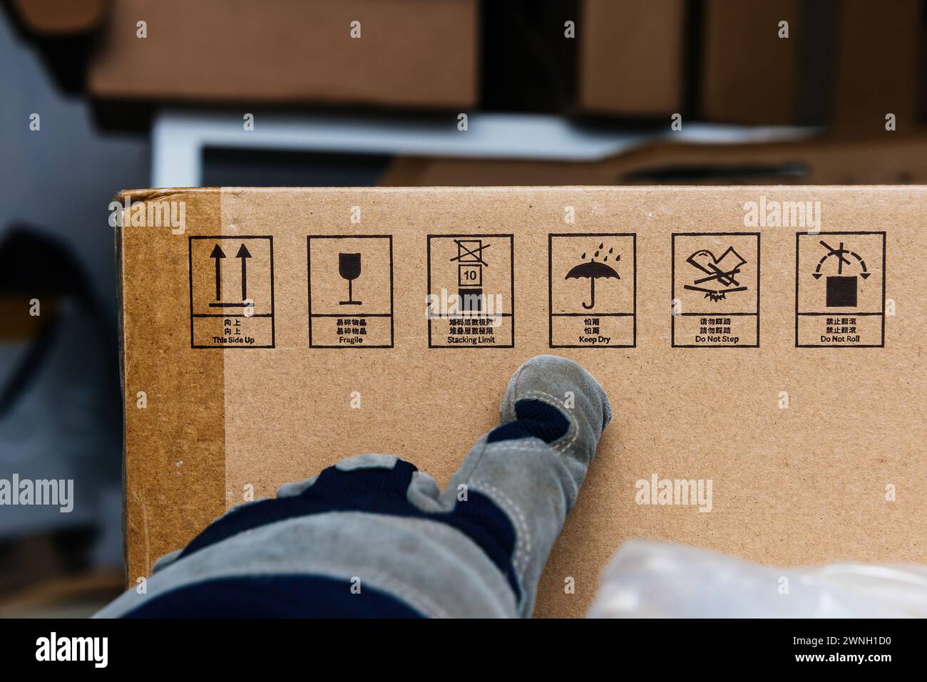 In a warehouse, a male worker wearing gloves points to cardboard boxes ...