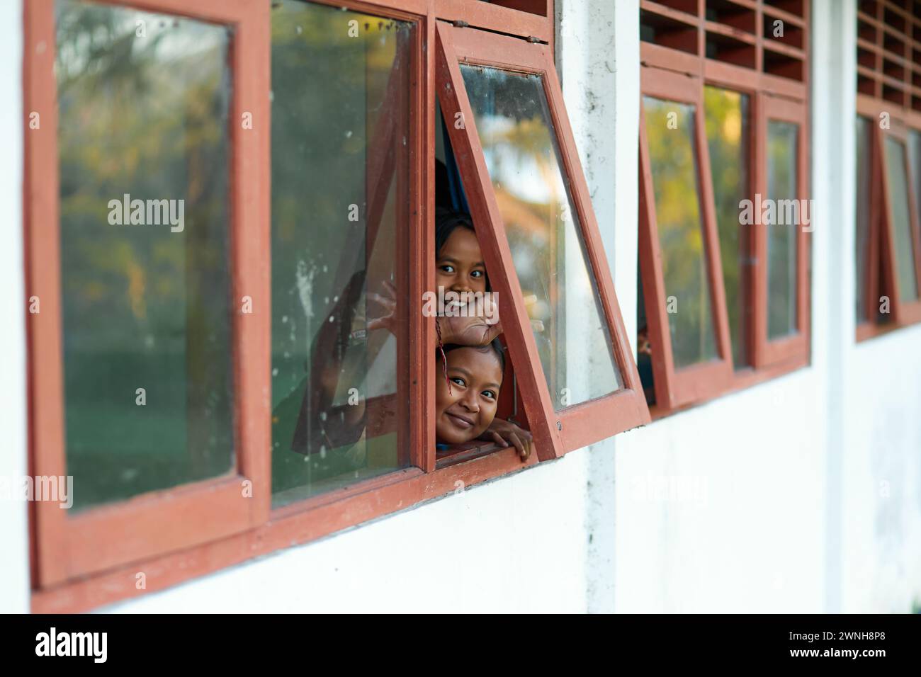 Happy little girls smile and look out of the window of a village school ...