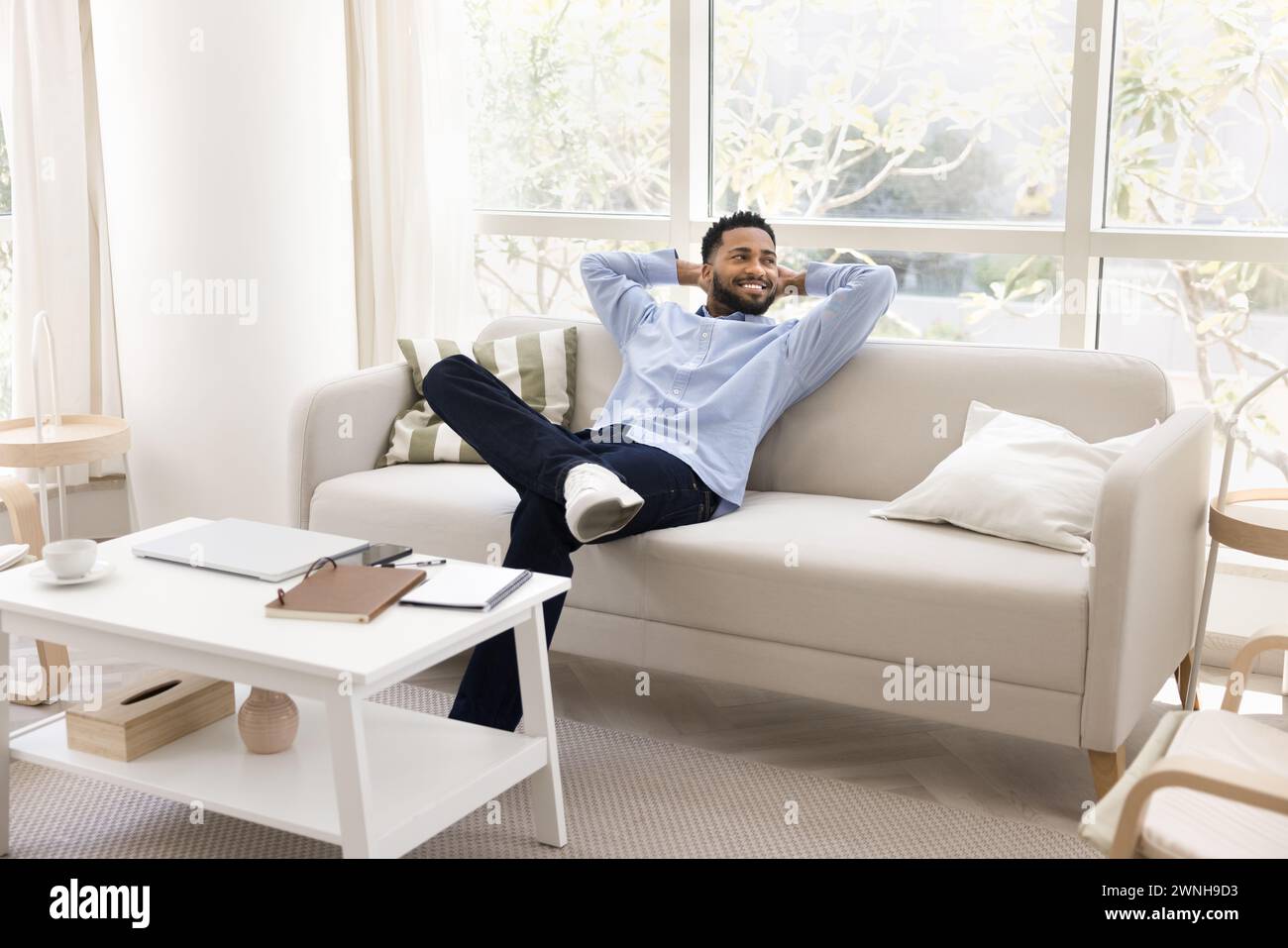 Cheerful young black freelance employee man stretching body on couch ...