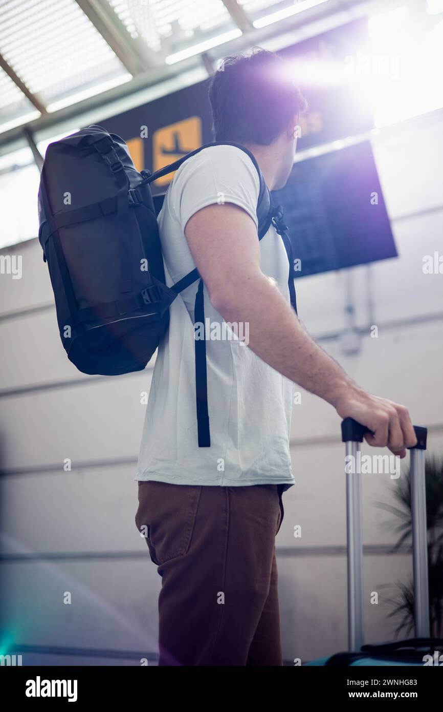 man with luggage standing in front of airport screens looking for his ...