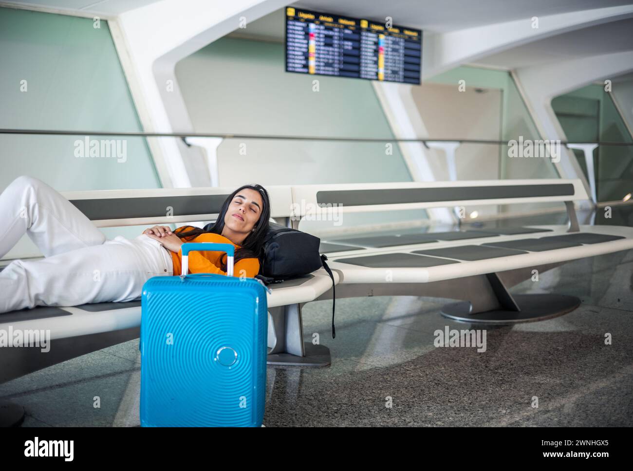 brunette girl sleeping on the airport benches while waiting for her flight with her luggage ...