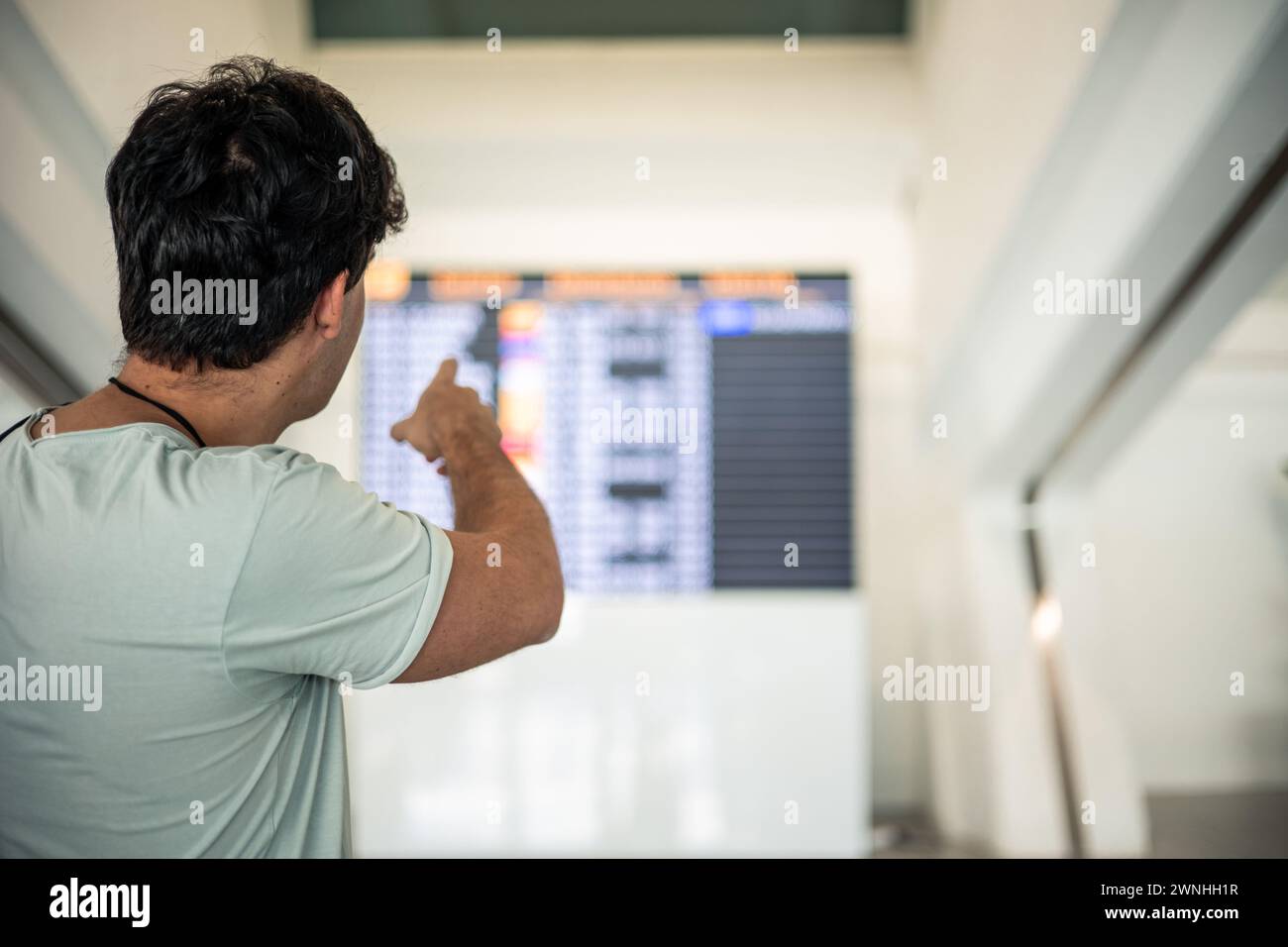 Traveler man photographed from behind pointing at terminal information ...