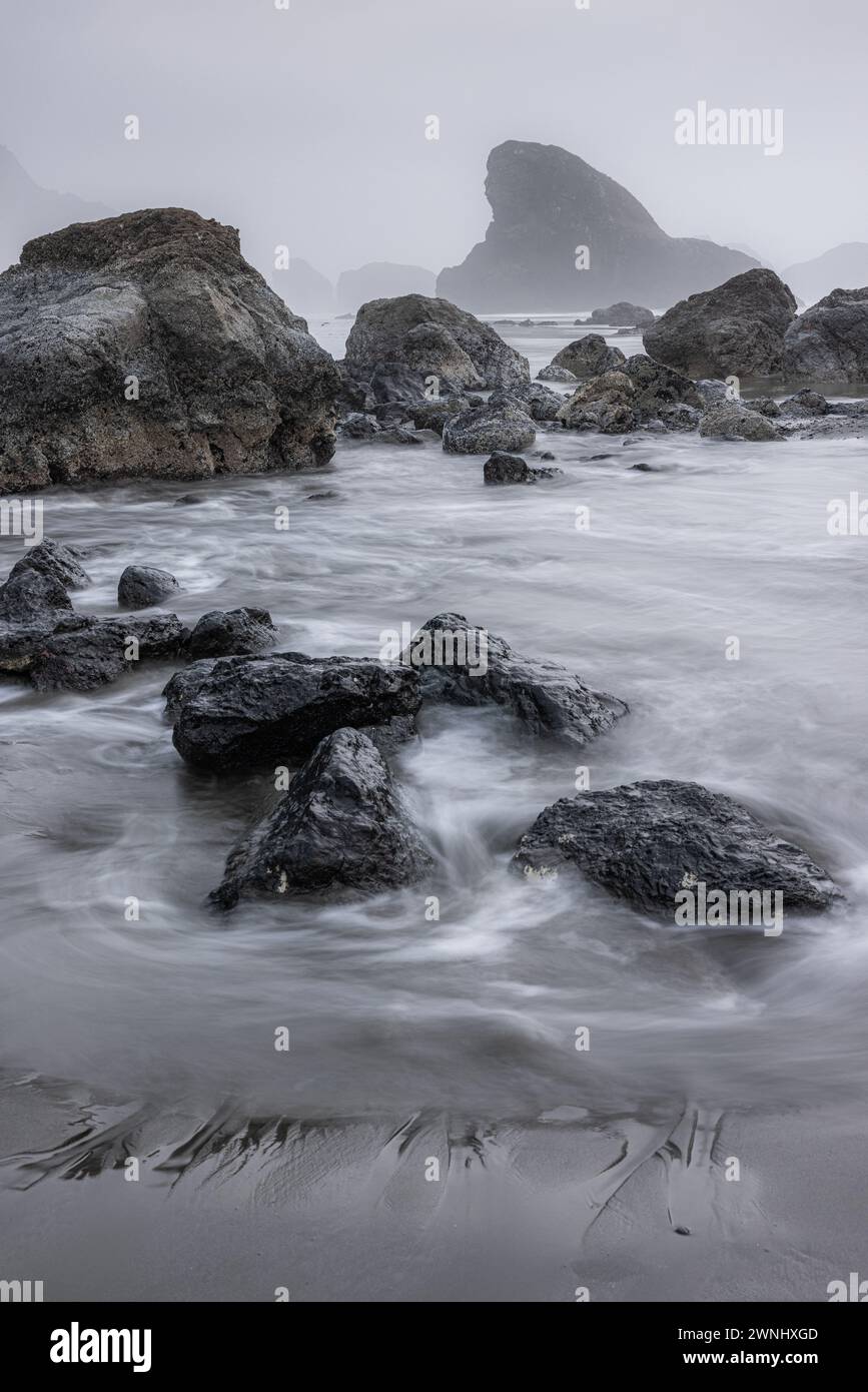 A rocky shoreline with a large rock in the distance. The water is calm ...