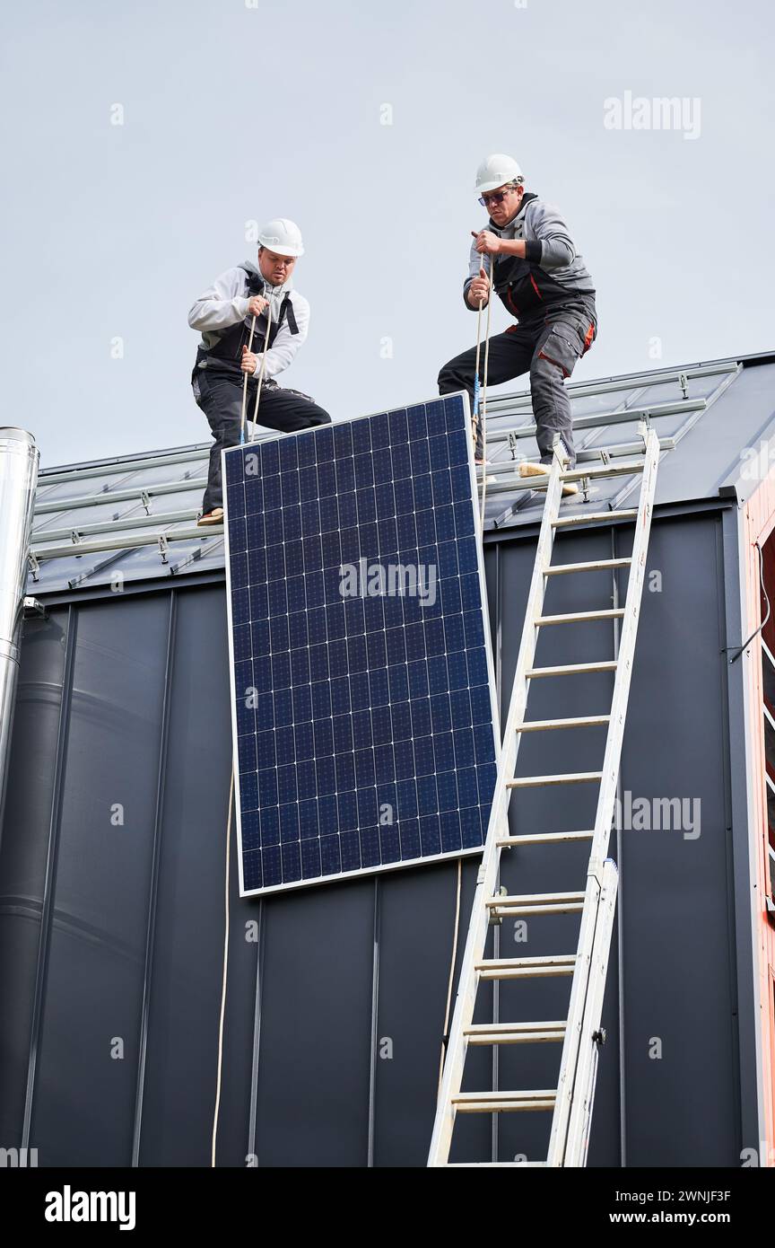 Men builders installing solar panel system on roof of house ...