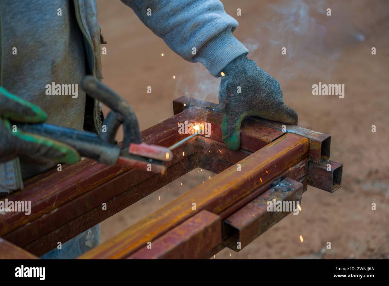 Welder welding two iron profiles at the construction site on a sunny ...