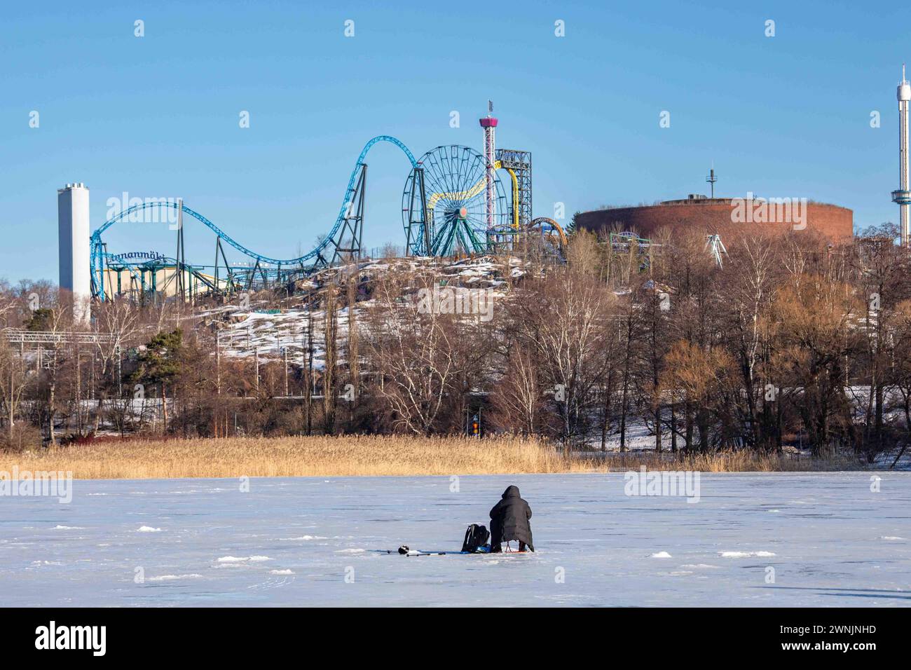 Man ice fishing on frozen Töölönlahti Bay with Linnanmäki amusement ...