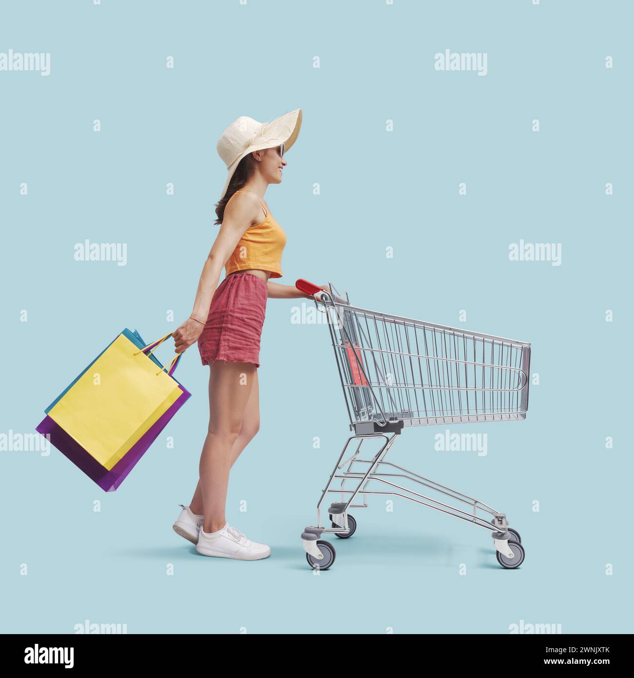 Young woman pushing an empty shopping cart, holding shopping bags and ...