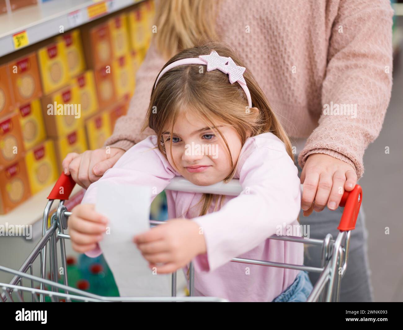 Disappointed girl at the supermarket with her mother, she is holding a ...