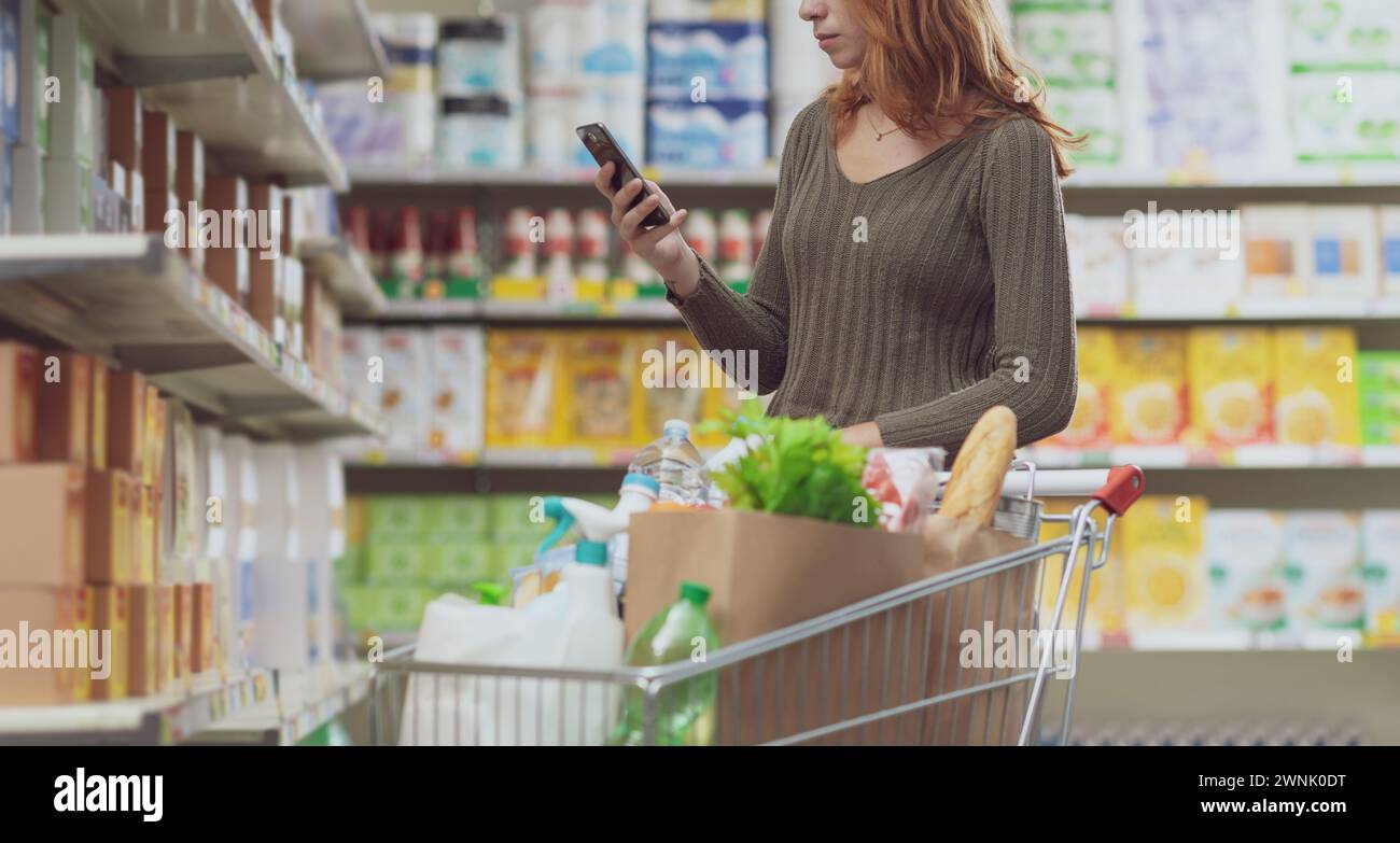 Young woman doing grocery shopping at the supermarket, she is checking ...