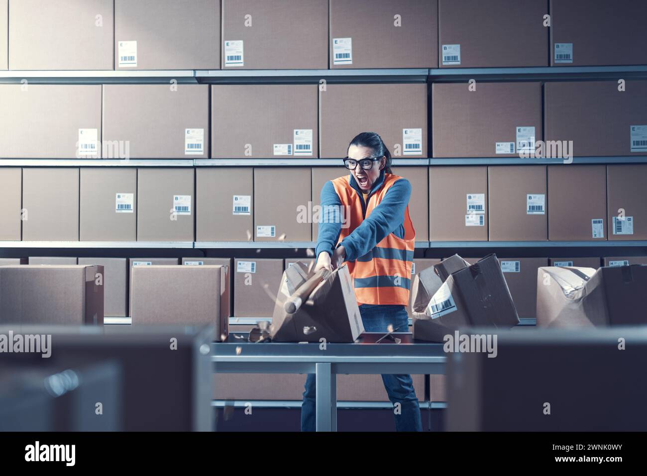 Aggressive rebellious warehouse worker smashing boxes at work, she is ...