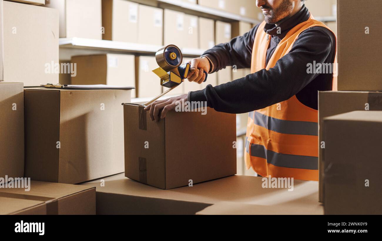 Warehouse worker sealing a cardboard box with adhesive tape, logistics ...