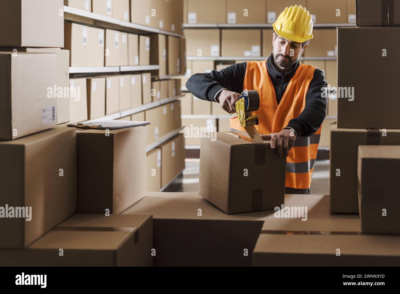 Warehouse worker sealing a cardboard box with adhesive tape, logistics ...