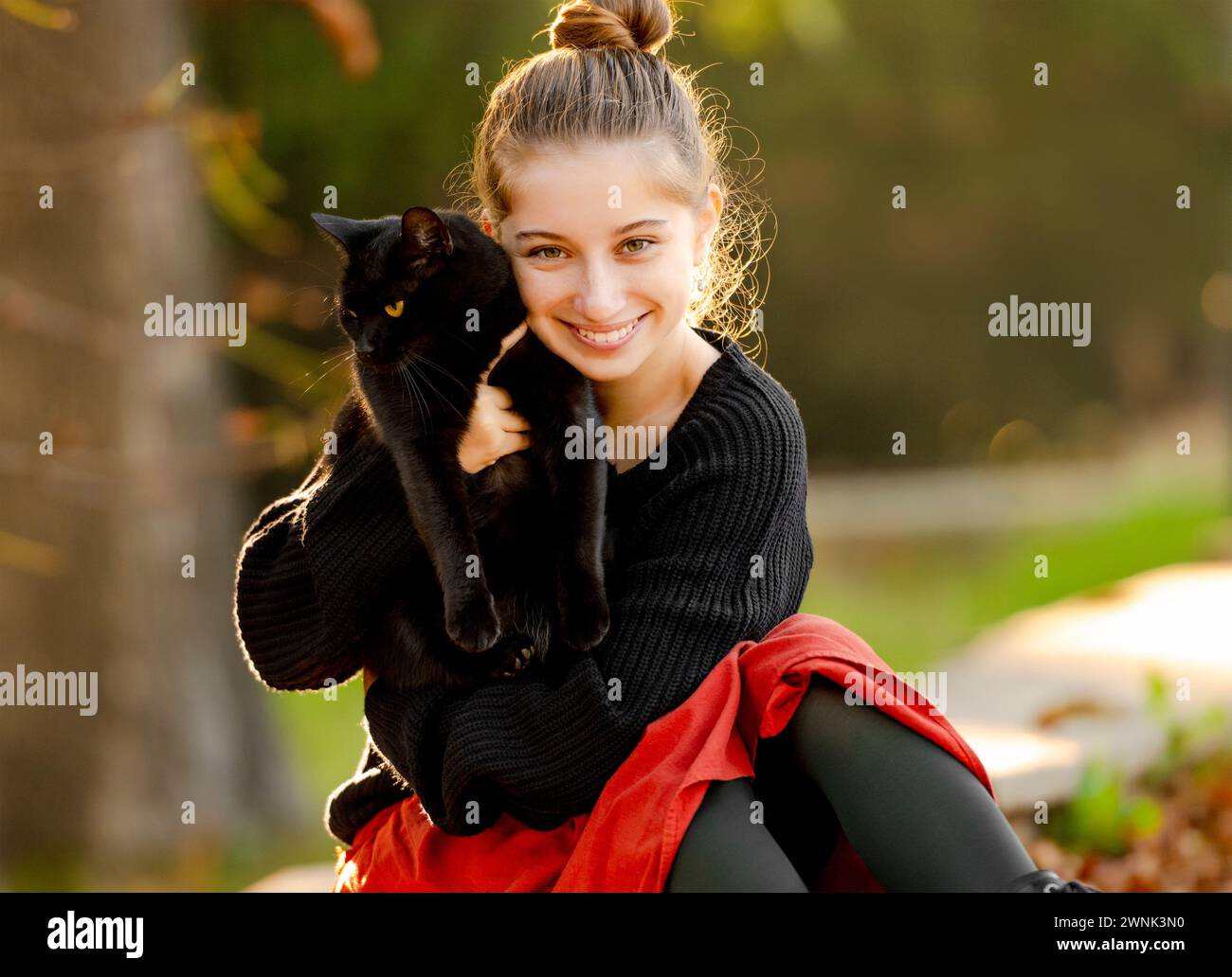 Pretty girl hugging black cat outdoors at street with autumn leaves ...