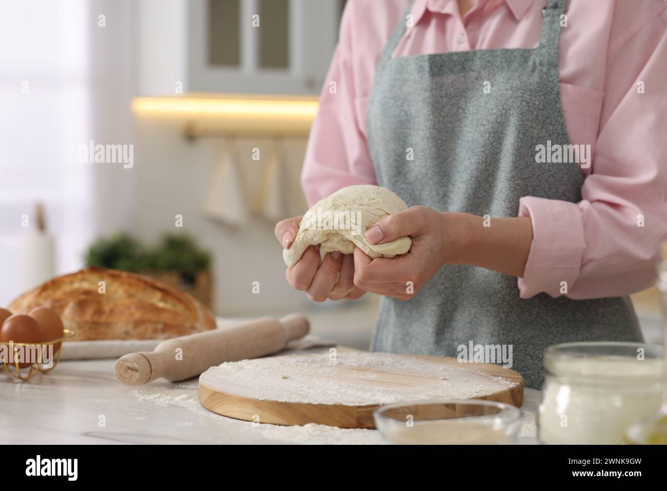 Making bread. Woman kneading dough at white table in kitchen, closeup ...