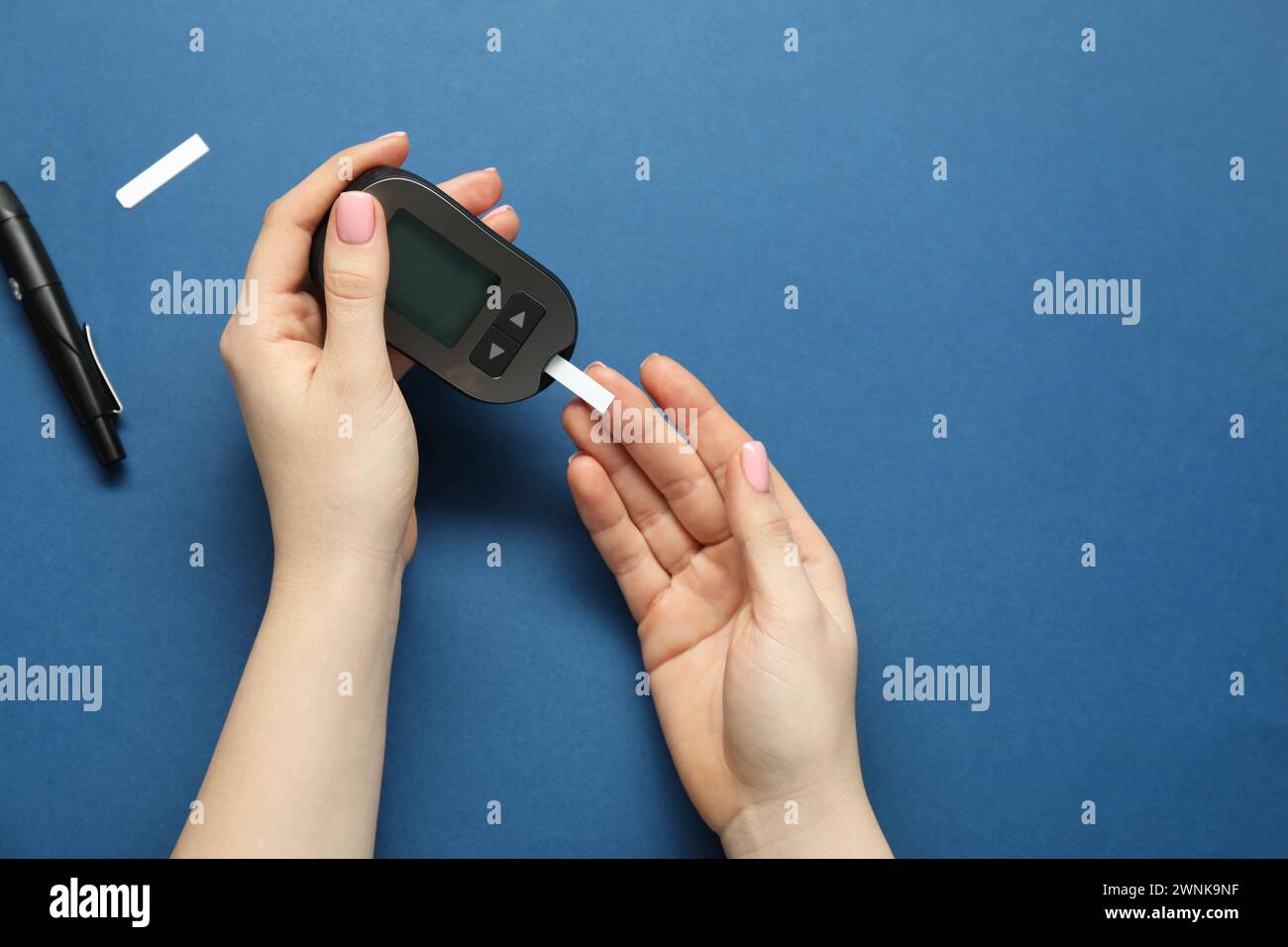 Diabetes. Woman checking blood sugar level with glucometer on blue ...