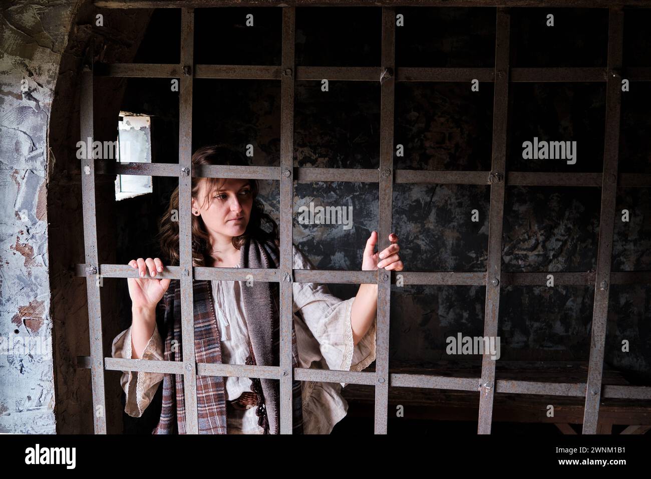 The girl prisoner looks longingly through the bars. A room in a dark ...