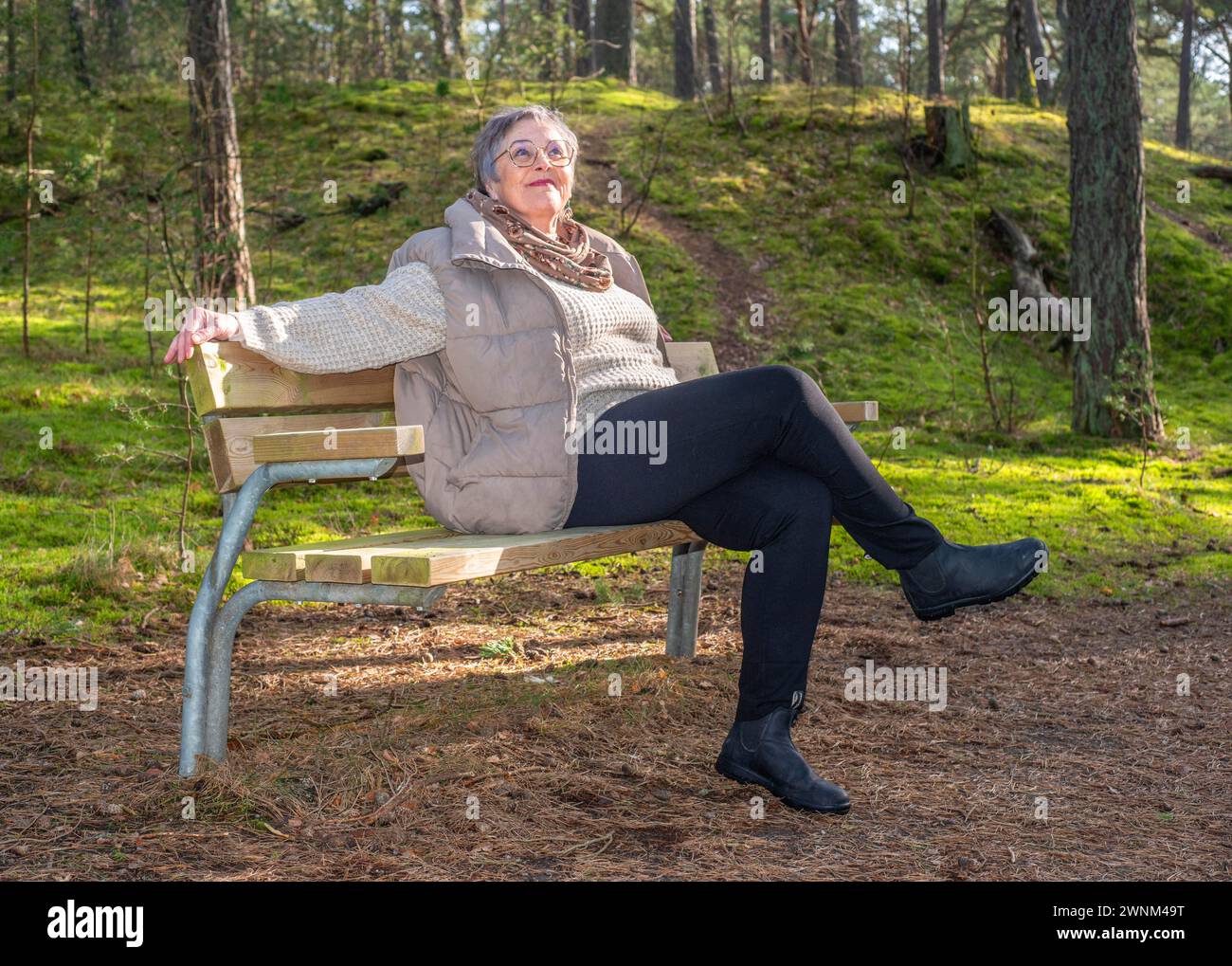 Elderly woman, 65 years old, sitting on a bench and enjoying nature in ...