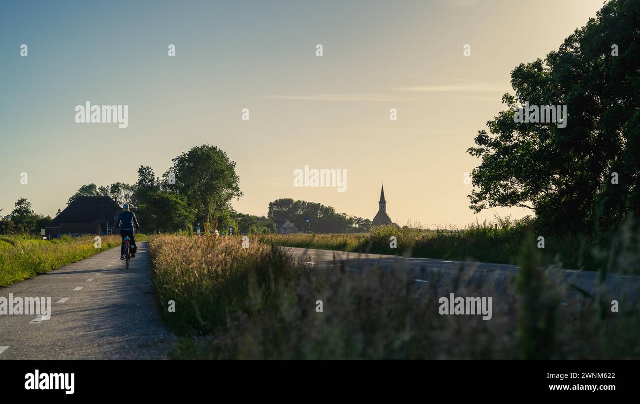 A cyclist rides along a rural road with a view of a church tower in the ...