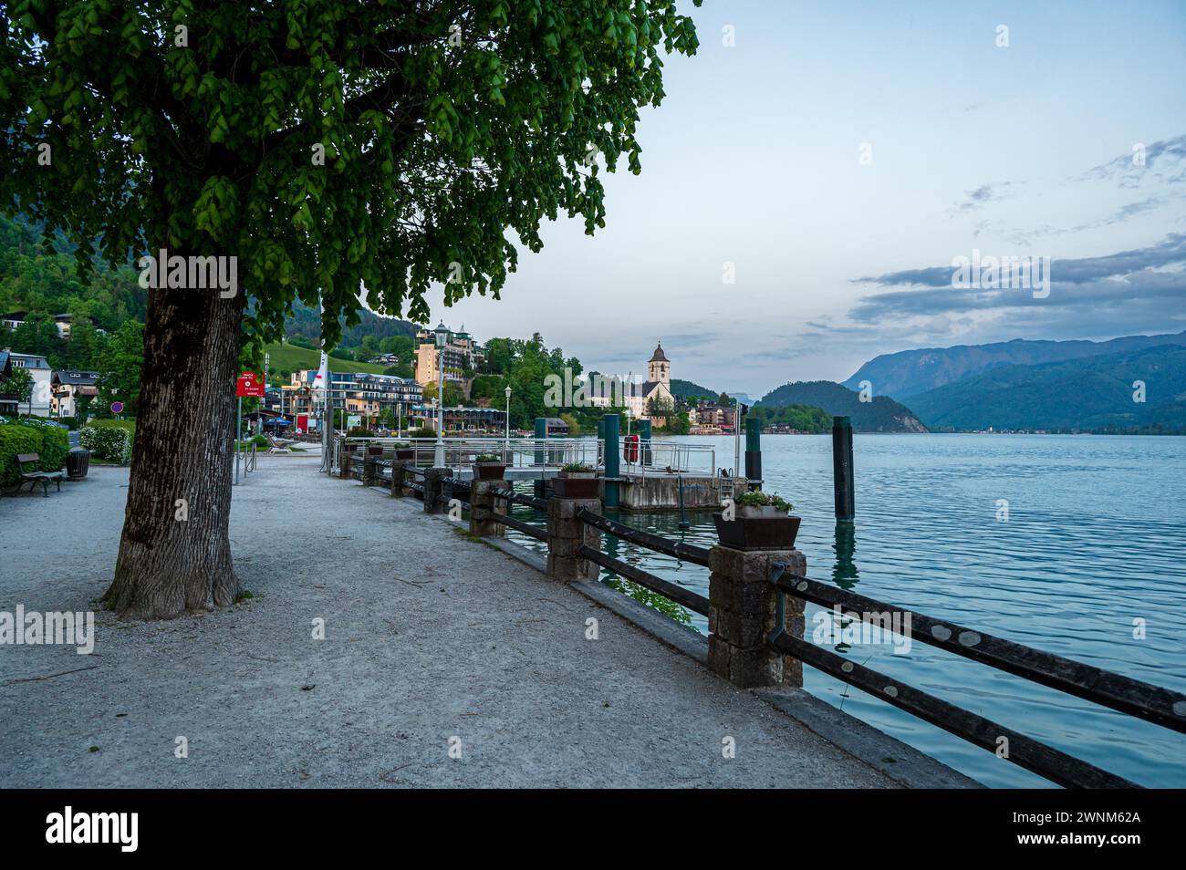 A lakeside path along a lake with trees and a view of a small town at ...