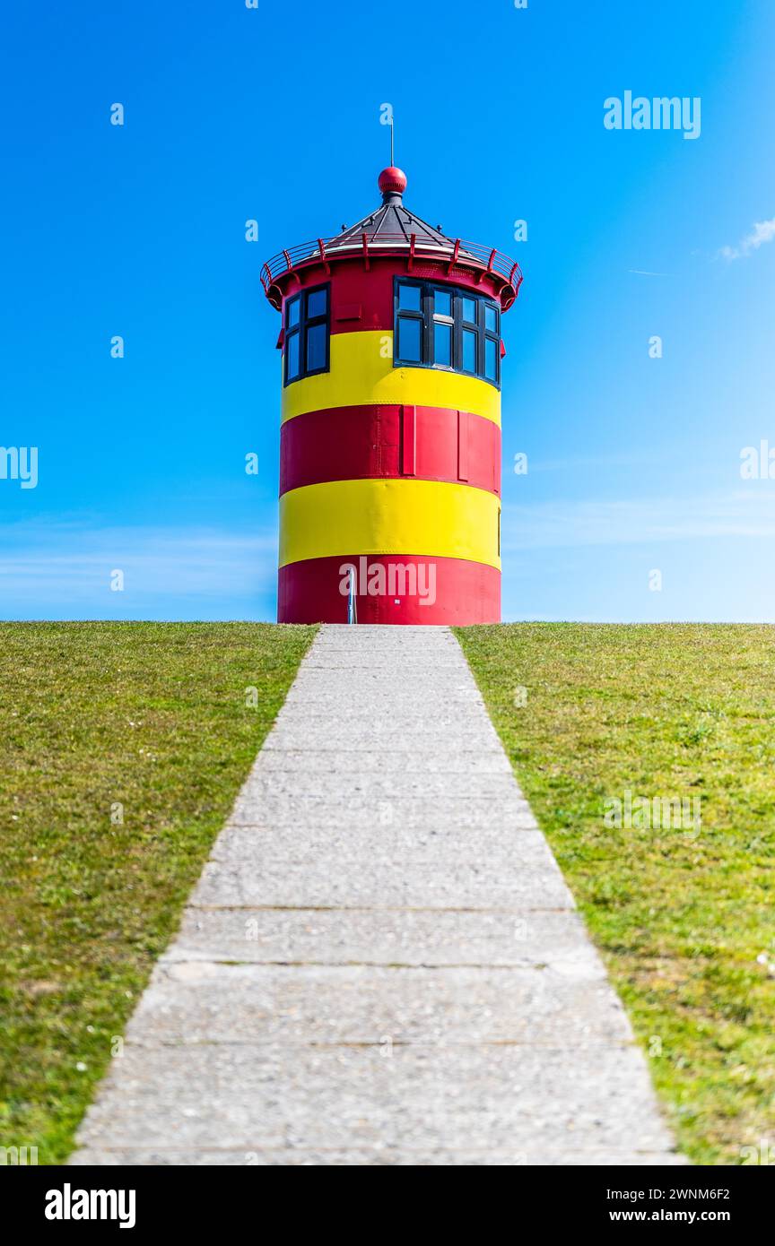 Path leads to a red-yellow lighthouse under a blue sky with loose ...