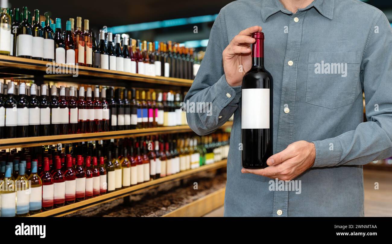 Man consumer standing in liquor supermarket and holding red wine bottle ...