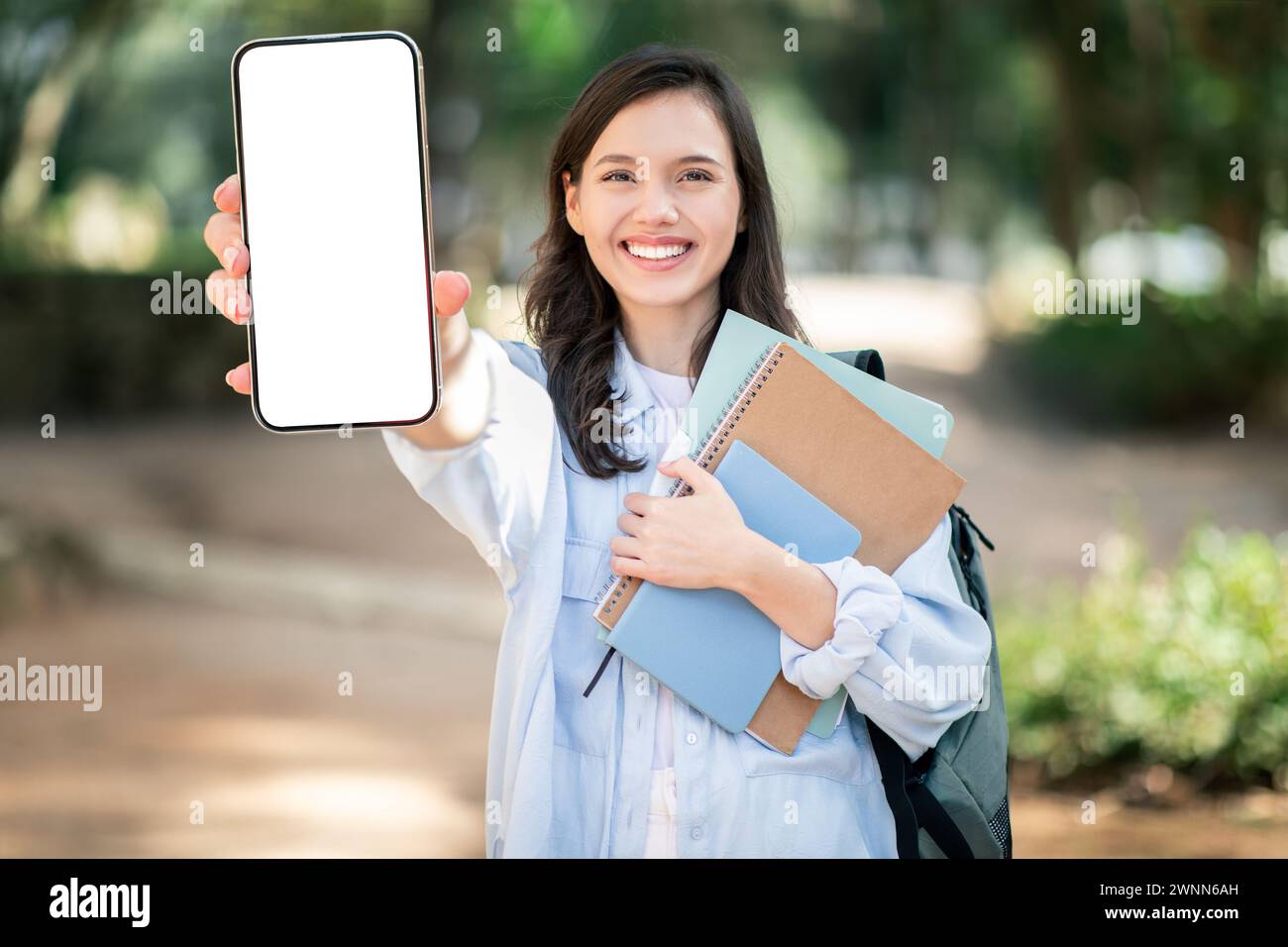 A cheerful young student shows her smartphone screen while holding ...