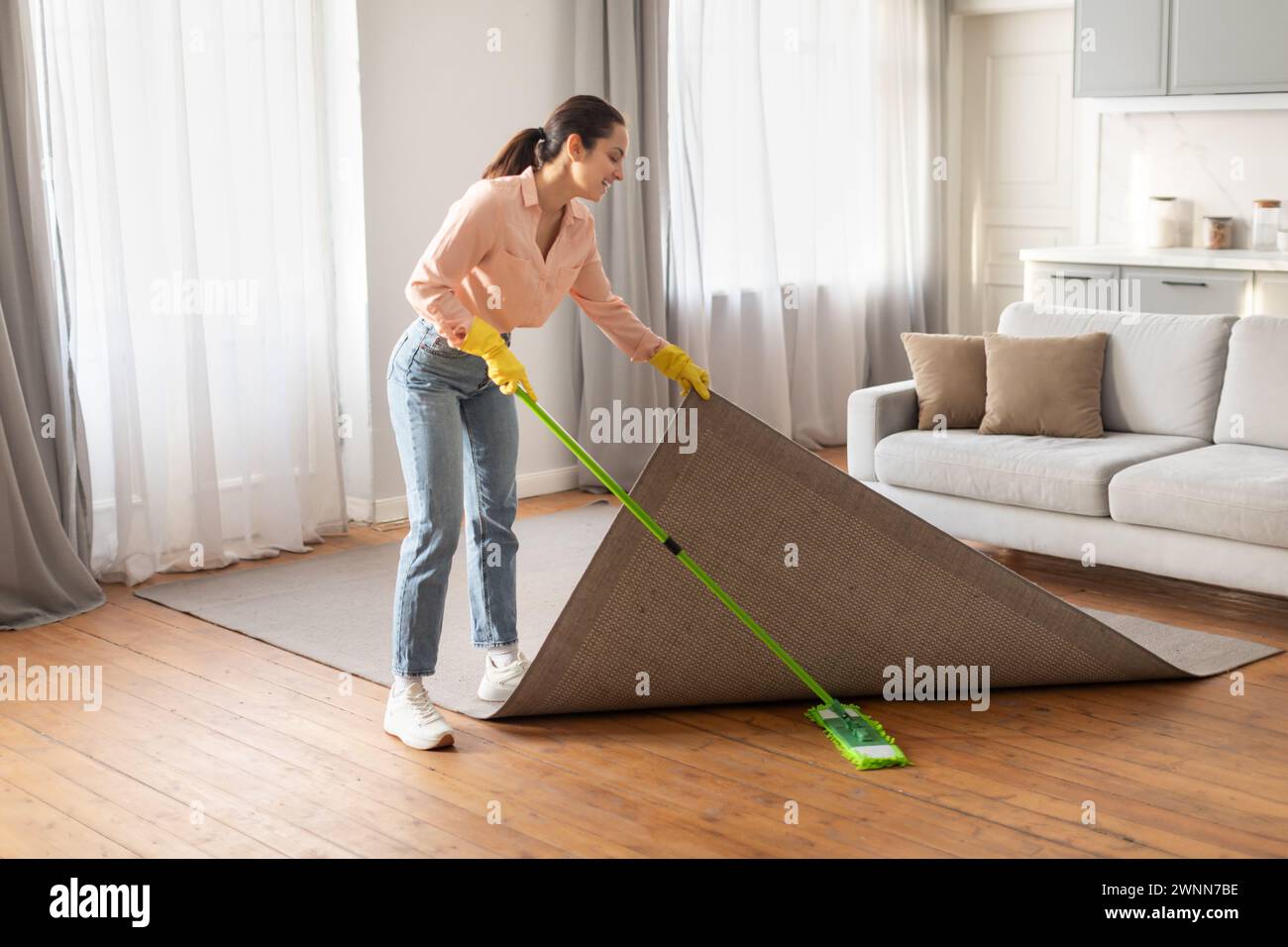 Focused woman lifting rug to clean underneath with mop Stock Photo - Alamy
