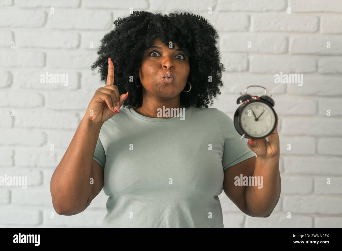 Surprised african american woman holding alarm clock amazed with open ...