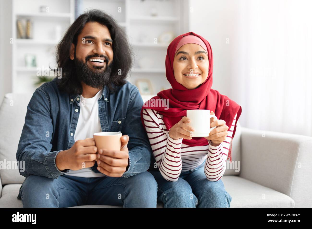 Happy Muslim Couple Drinking Coffee And Relaxing On Couch In Living ...