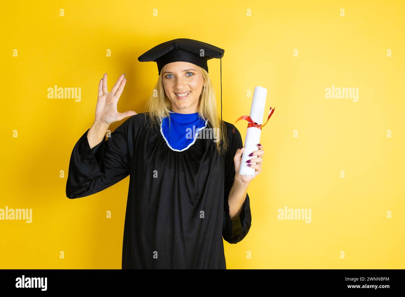 Beautiful blonde young woman wearing graduation cap and ceremony robe ...